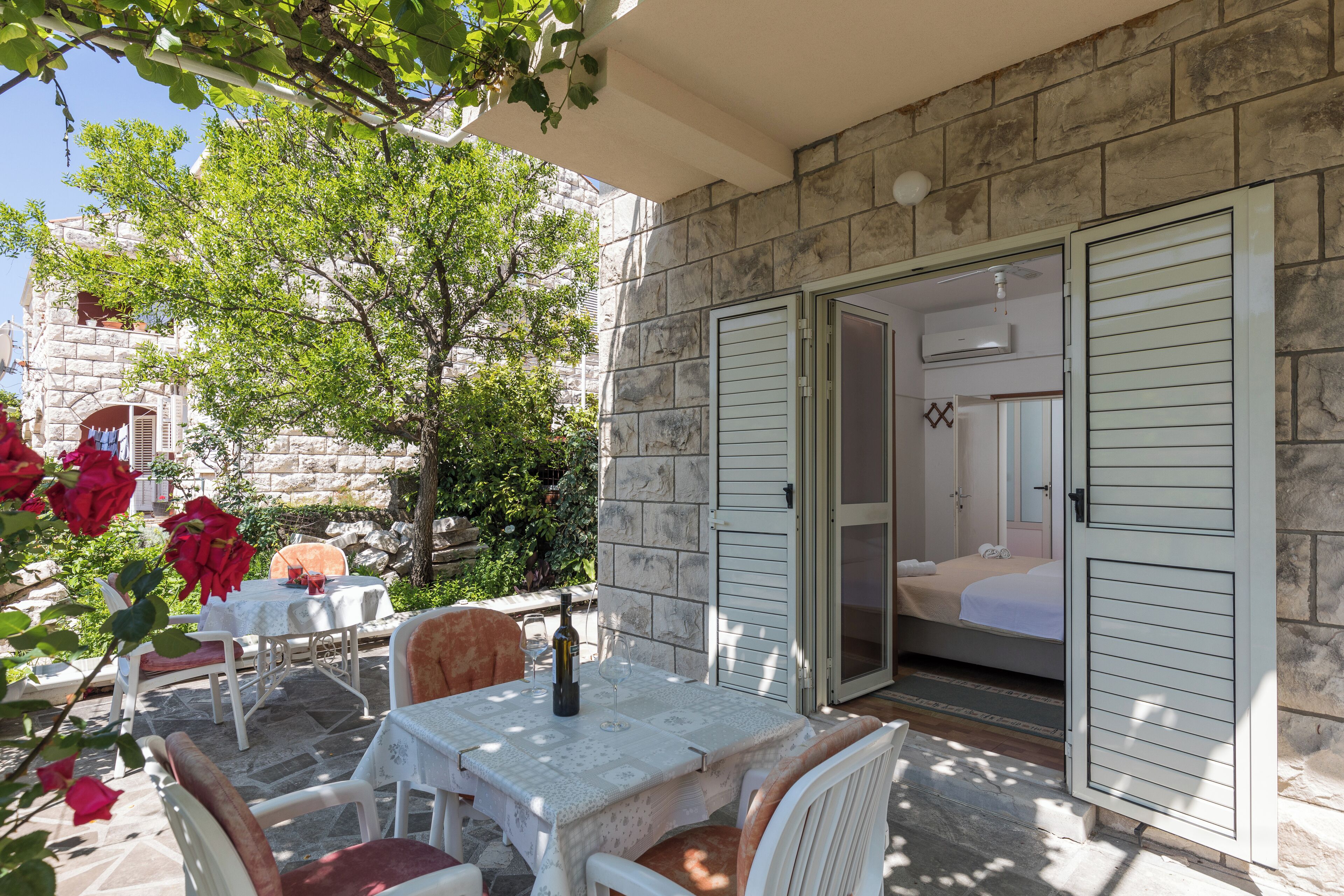 Um pátio externo com mesa e cadeiras, uma parede de pedra e um quarto com cama e portas de correr.