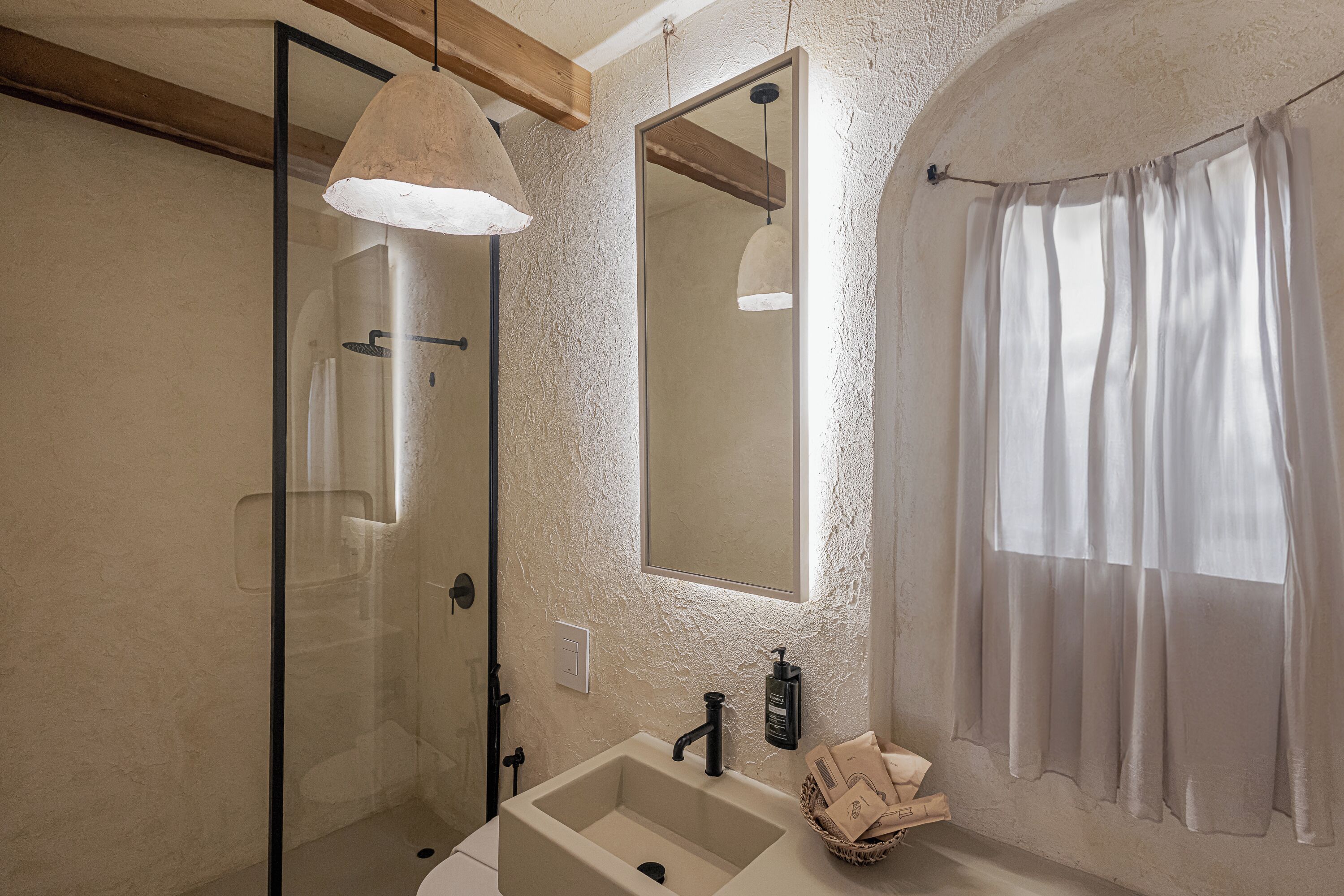 Uma casa de banho com cabine de duche em vidro, lavatório com espelho e janela com cortinas.