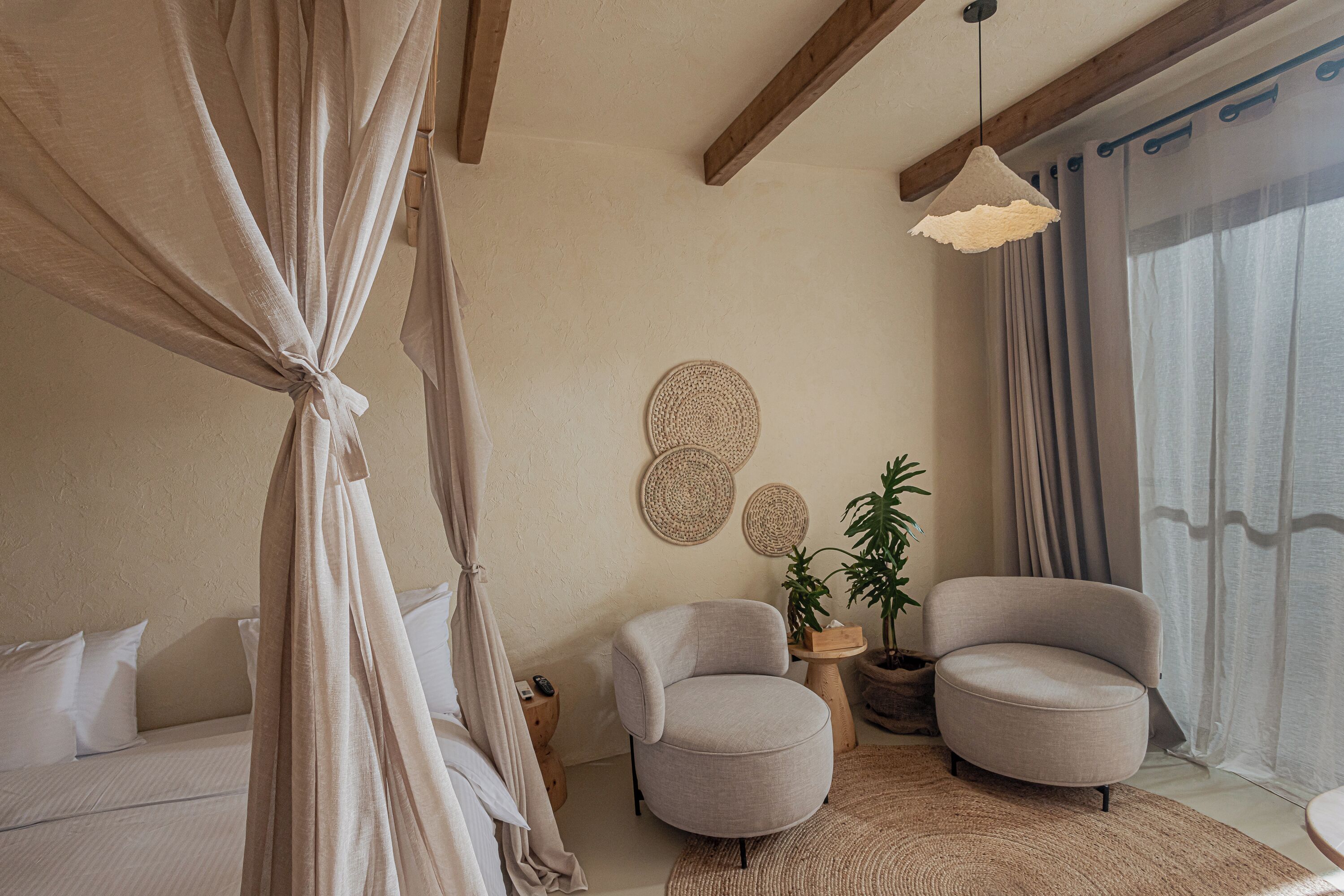 Quarto com cama de dossel, duas poltronas, uma mesinha com uma planta e um candeeiro suspenso.
