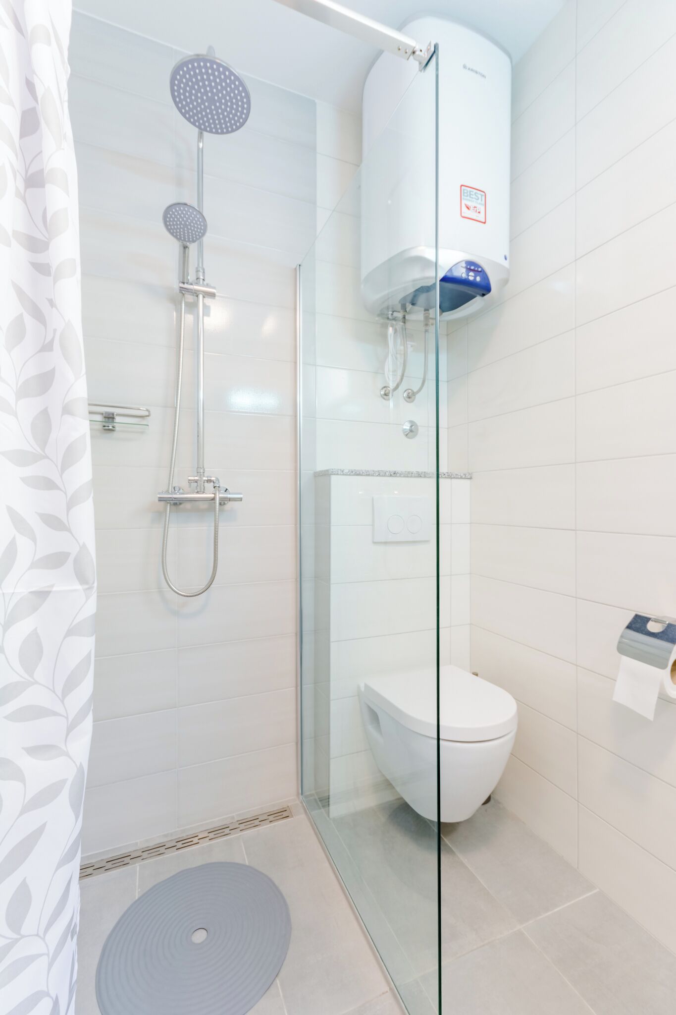 Uma casa de banho moderna com chuveiro em cabine de vidro, sanita branca e aquecedor fixado na parede.
