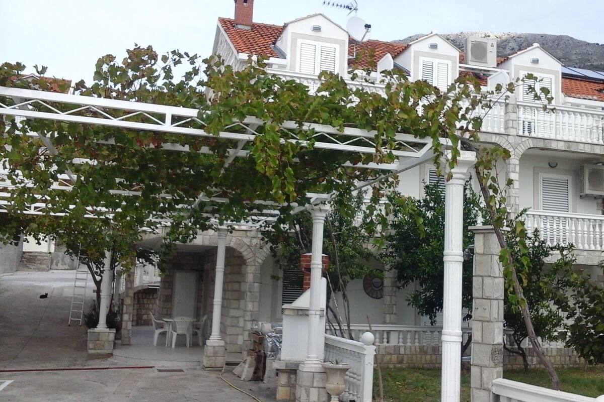 Um edifício residencial com fachada de pedra, varandas brancas e uma pérgula coberta de plantas trepadoras.