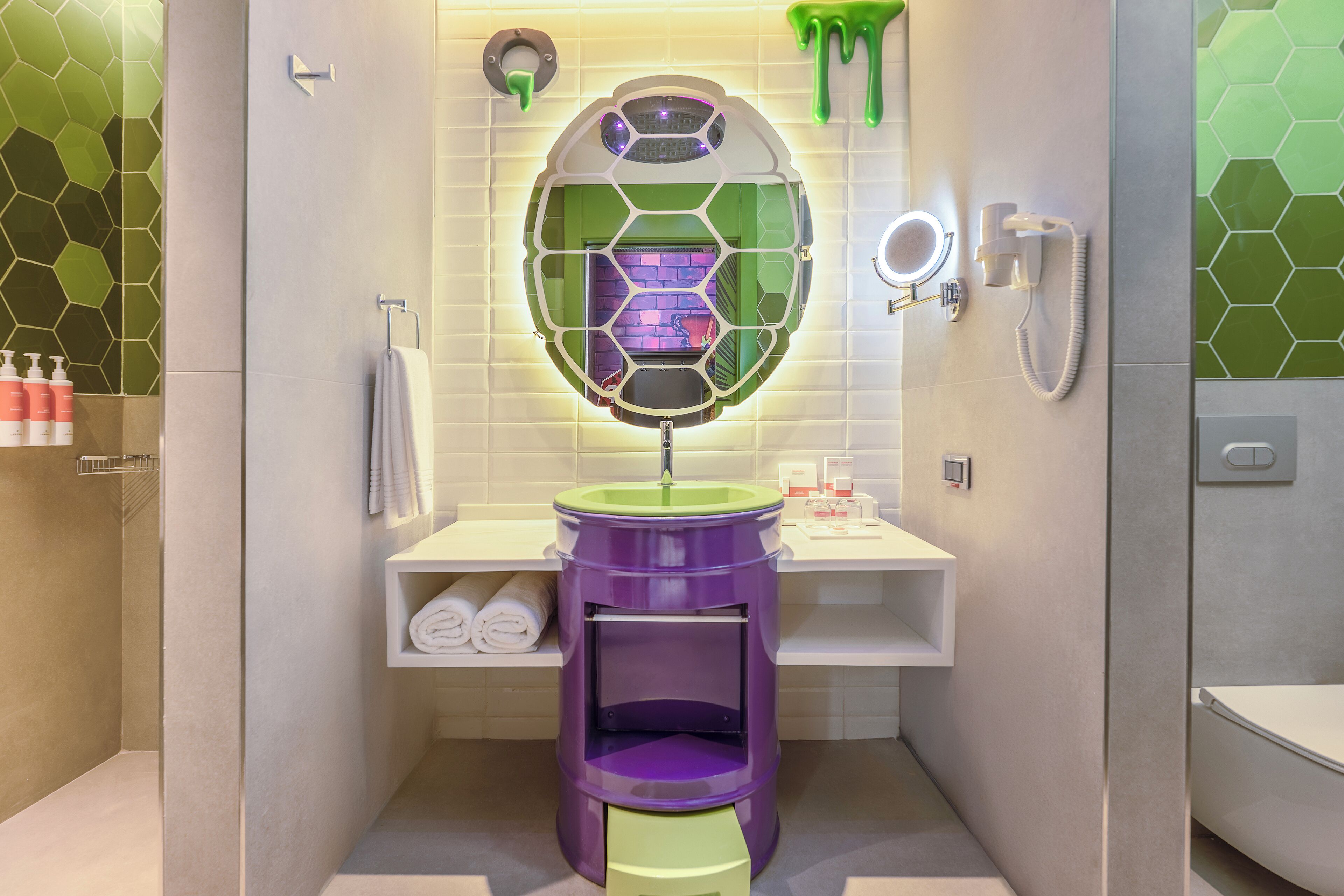 Uma casa de banho com design moderno, apresentando um espelho hexagonal exclusivo, uma pia roxa e verde, e uma área de duche.