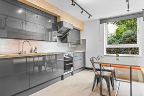 Cozinha moderna com bancada de madeira, eletrodomésticos de aço inoxidável e área de refeições com mesa e cadeiras.