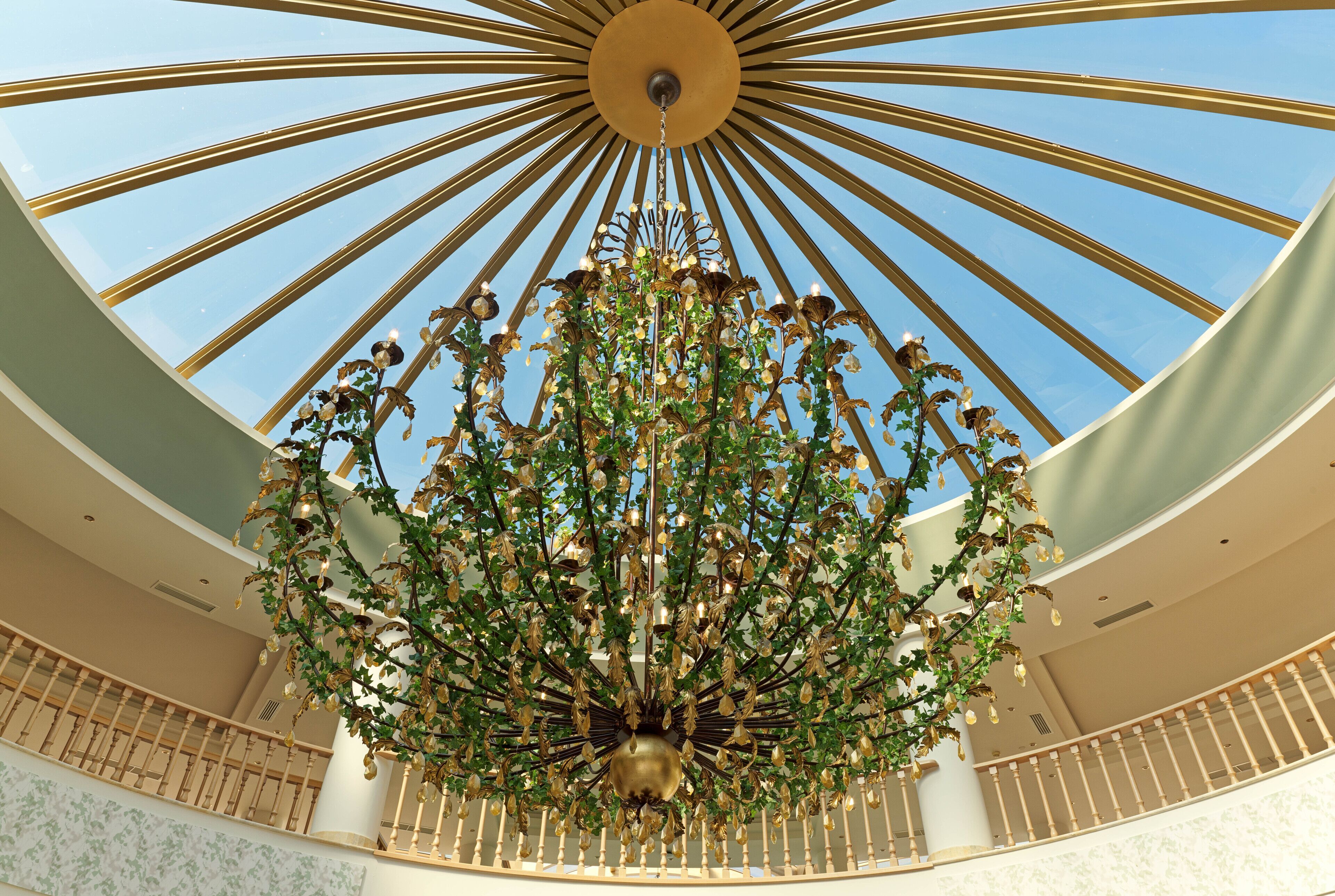 Um imponente candelabro com design radial, suspenso no alto de um teto em um amplo átrio com vista aberta para o céu.