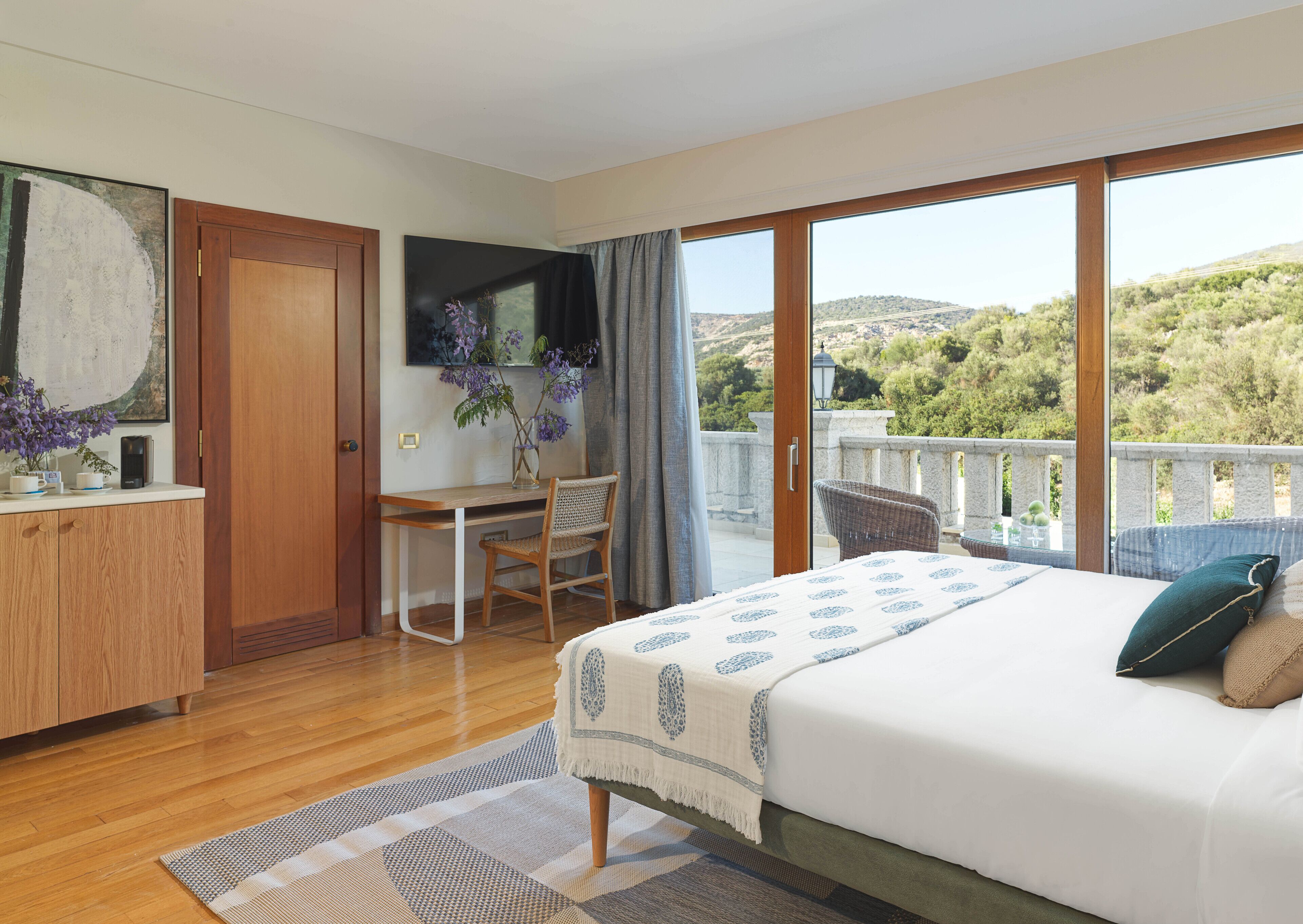 Quarto com cama grande, escrivaninha, cadeira e varanda com vista para o campo.