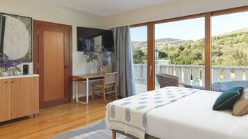 Quarto com cama grande, escrivaninha, cadeira e varanda com vista para o campo.