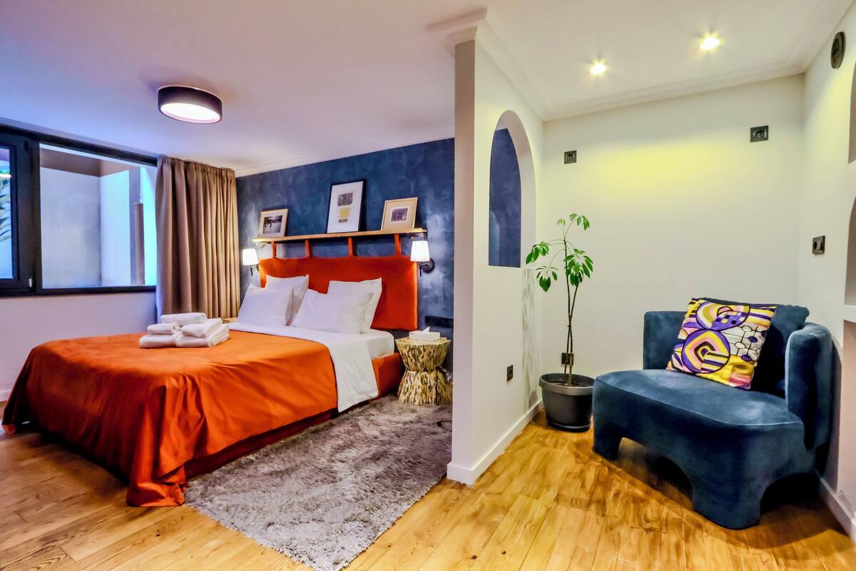 Quarto de hotel moderno com cama, uma cadeira, uma pequena mesa e um vaso de planta.