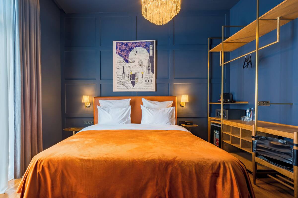Quarto de hotel moderno com uma cama grande, uma mesa de cabeceira de madeira, uma estante na parede e um candelabro.