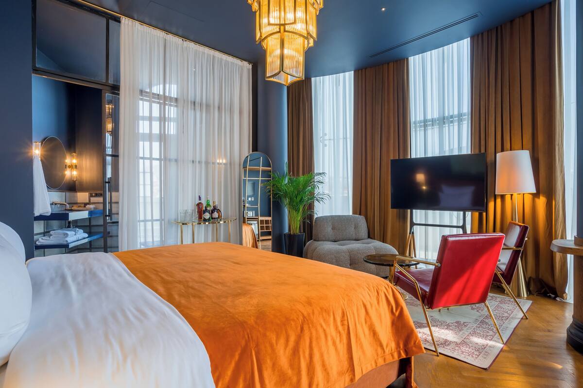 Quarto de hotel moderno com uma cama grande, uma escrivaninha, uma TV e um vaso de plantas.