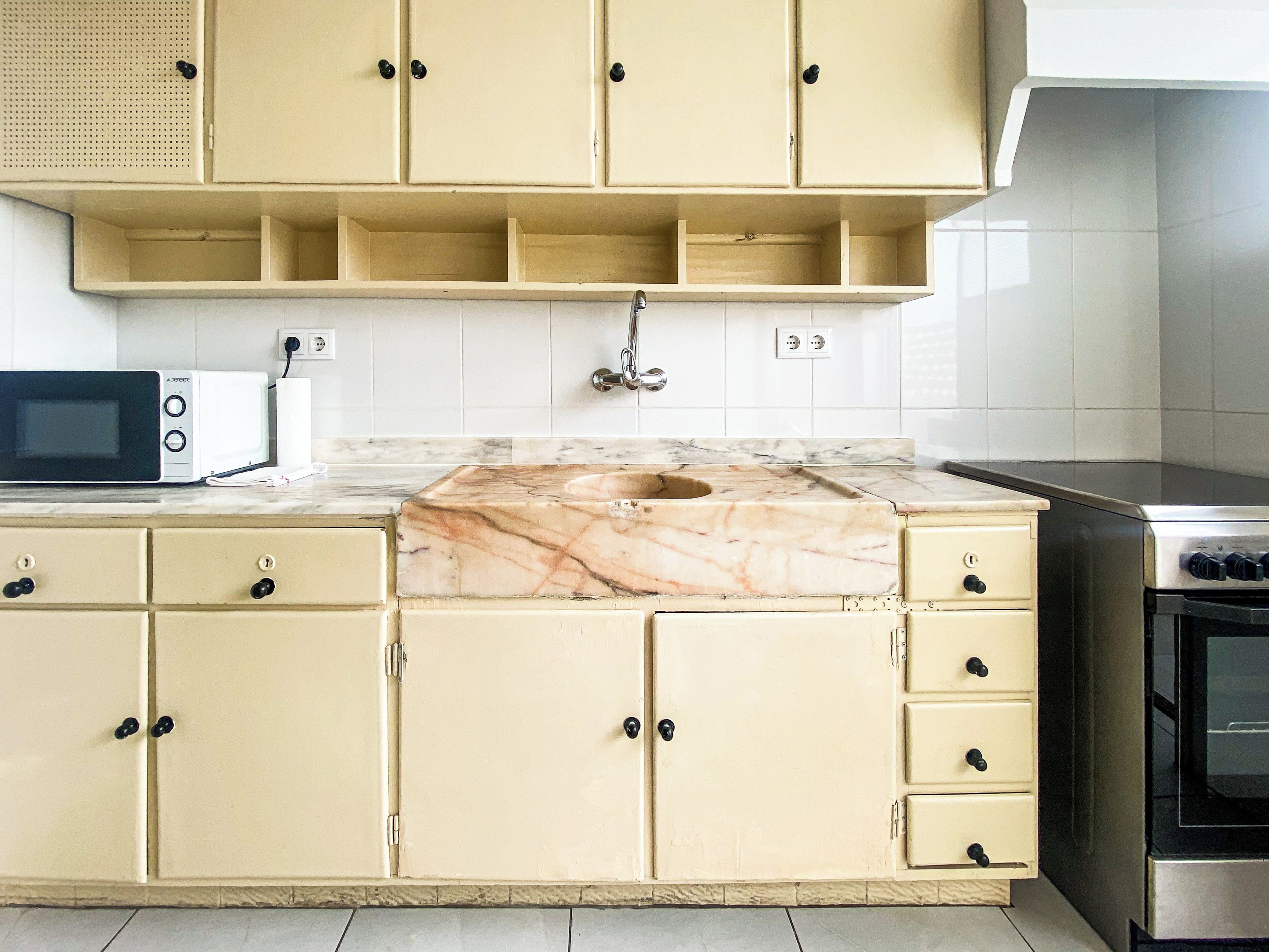 Uma cozinha com armários bege, bancada de mármore, micro-ondas e forno.