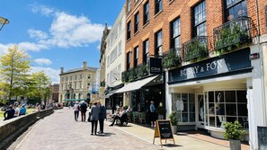 Uma rua de calçada com cafés e lojas, incluindo 'BUSBY & FOX' e 'CÔTE BRASSERIES'.
