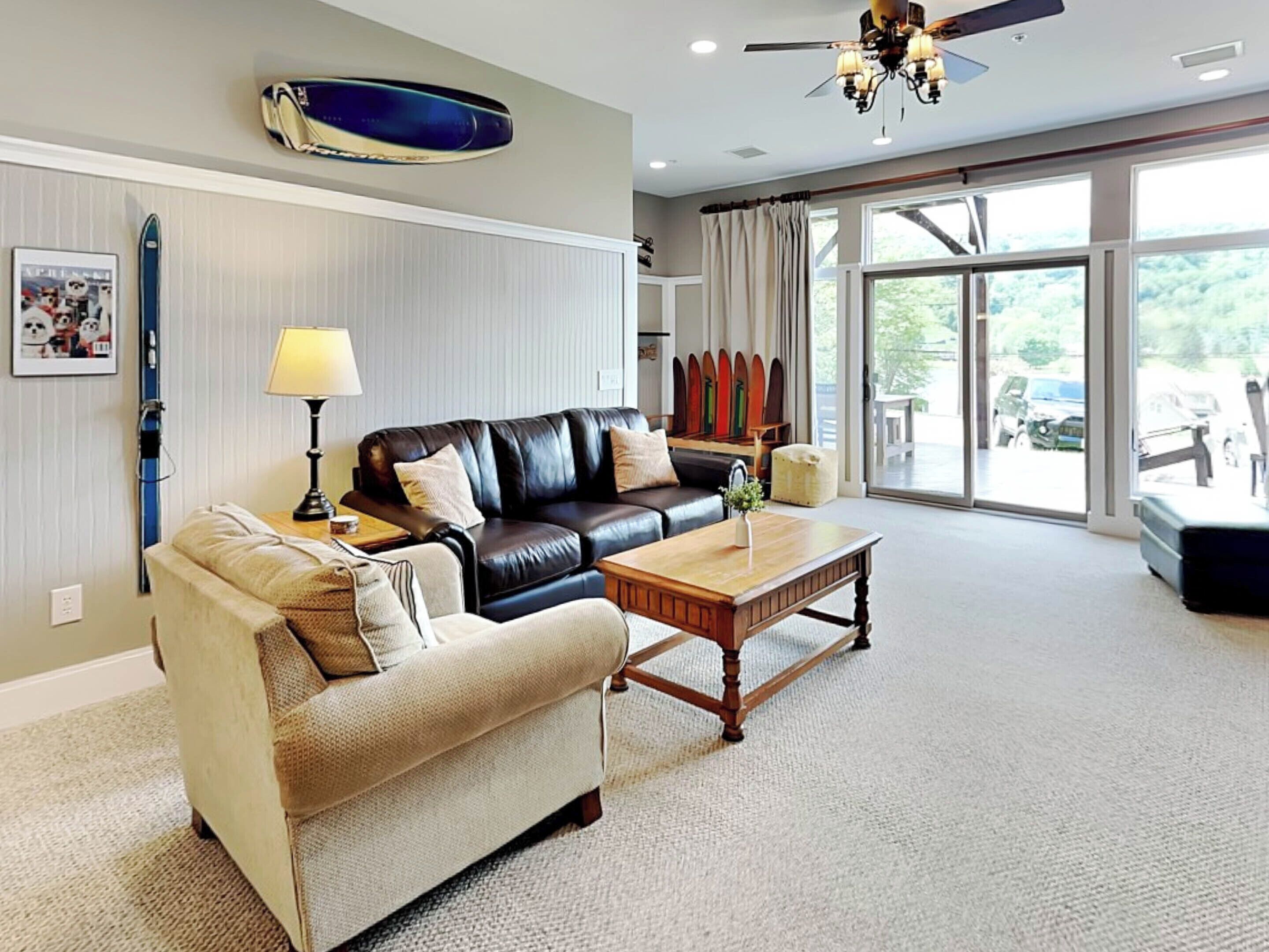 Sala de estar com sofá de couro, poltrona bege, mesa de centro de madeira e ventilador de teto.
