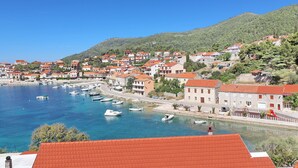 Uma cidade costeira com edifícios à beira-mar, barcos ancorados no porto e uma encosta ao fundo.