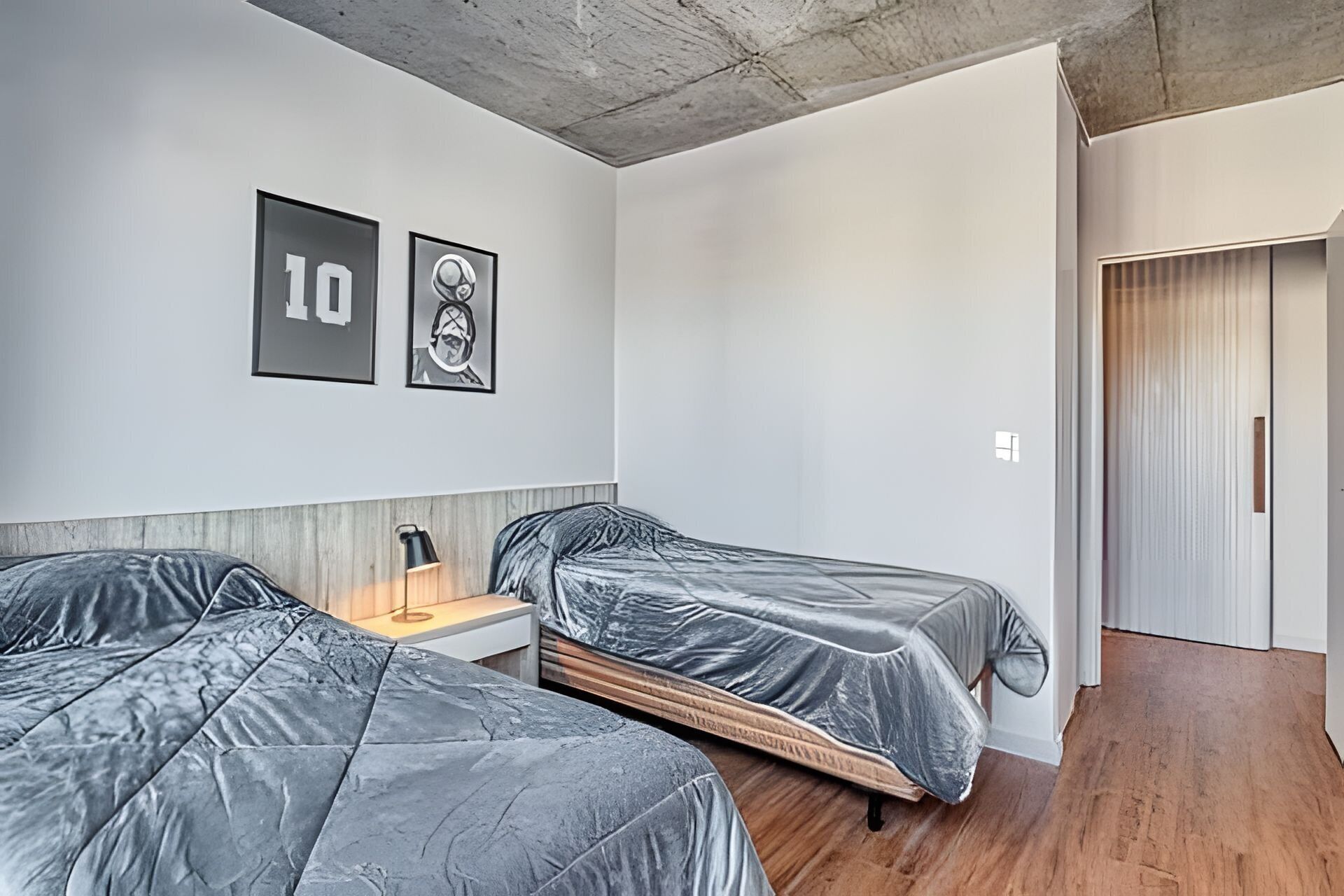 Quarto com duas camas, uma mesa de cabeceira e uma porta.