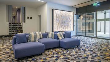Um hall moderno com um sofá modular azul, carpete estampado e uma grande obra de arte abstrata.