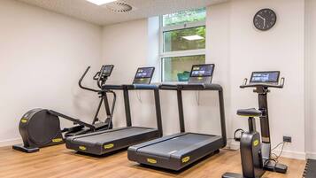 Sala de ginástica com três esteiras, um elíptico e uma bicicleta ergométrica, todos com mostradores digitais.