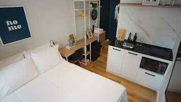 Quarto compacto com cama, cozinha compacta e pequena escrivaninha.