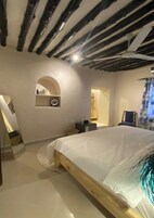 Quarto com cama de madeira, um espelho, prateleira com produtos de higiene pessoal e ventilador de teto.
