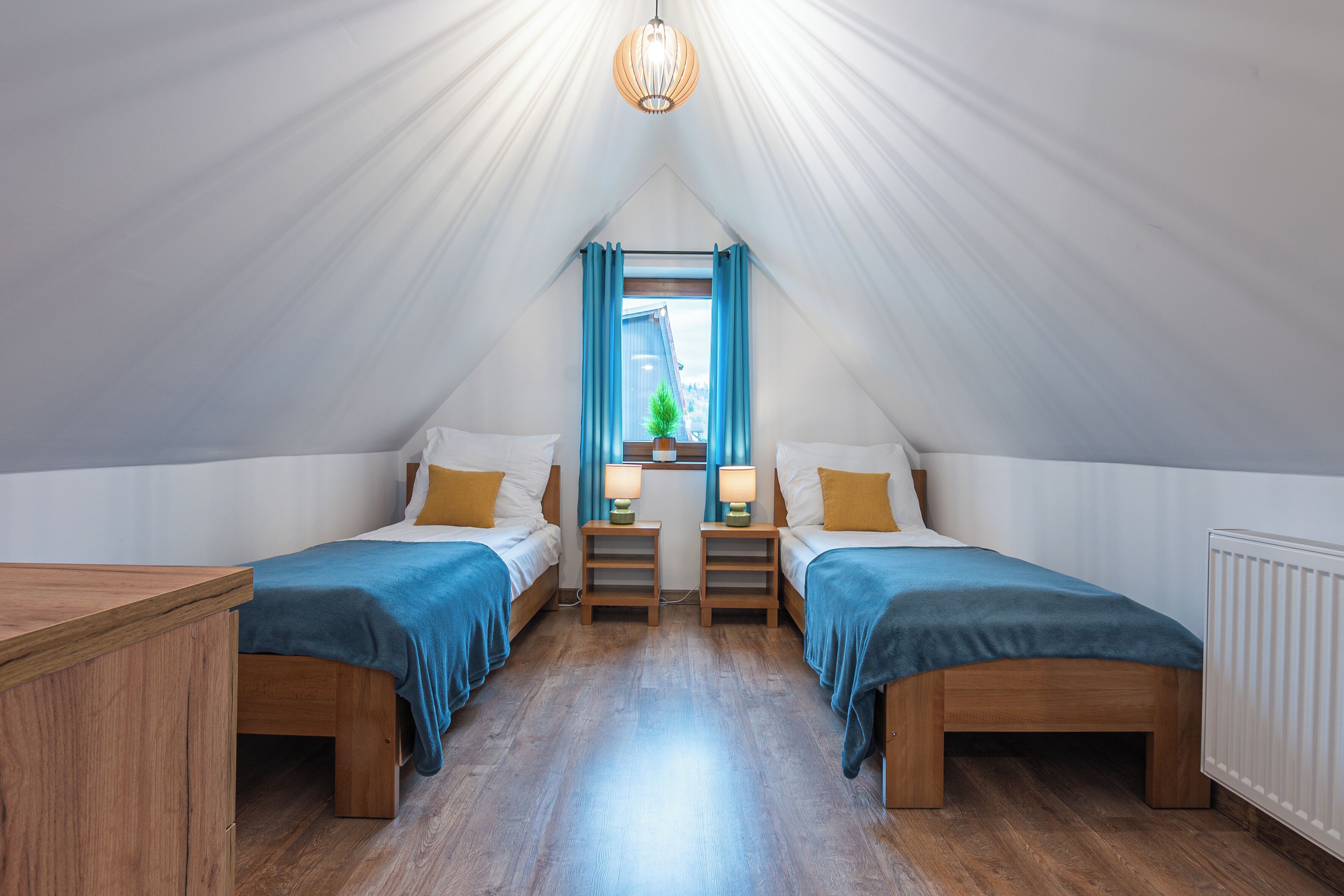 Quarto de sótão acolhedor com duas camas, piso de madeira e vista pela janela.