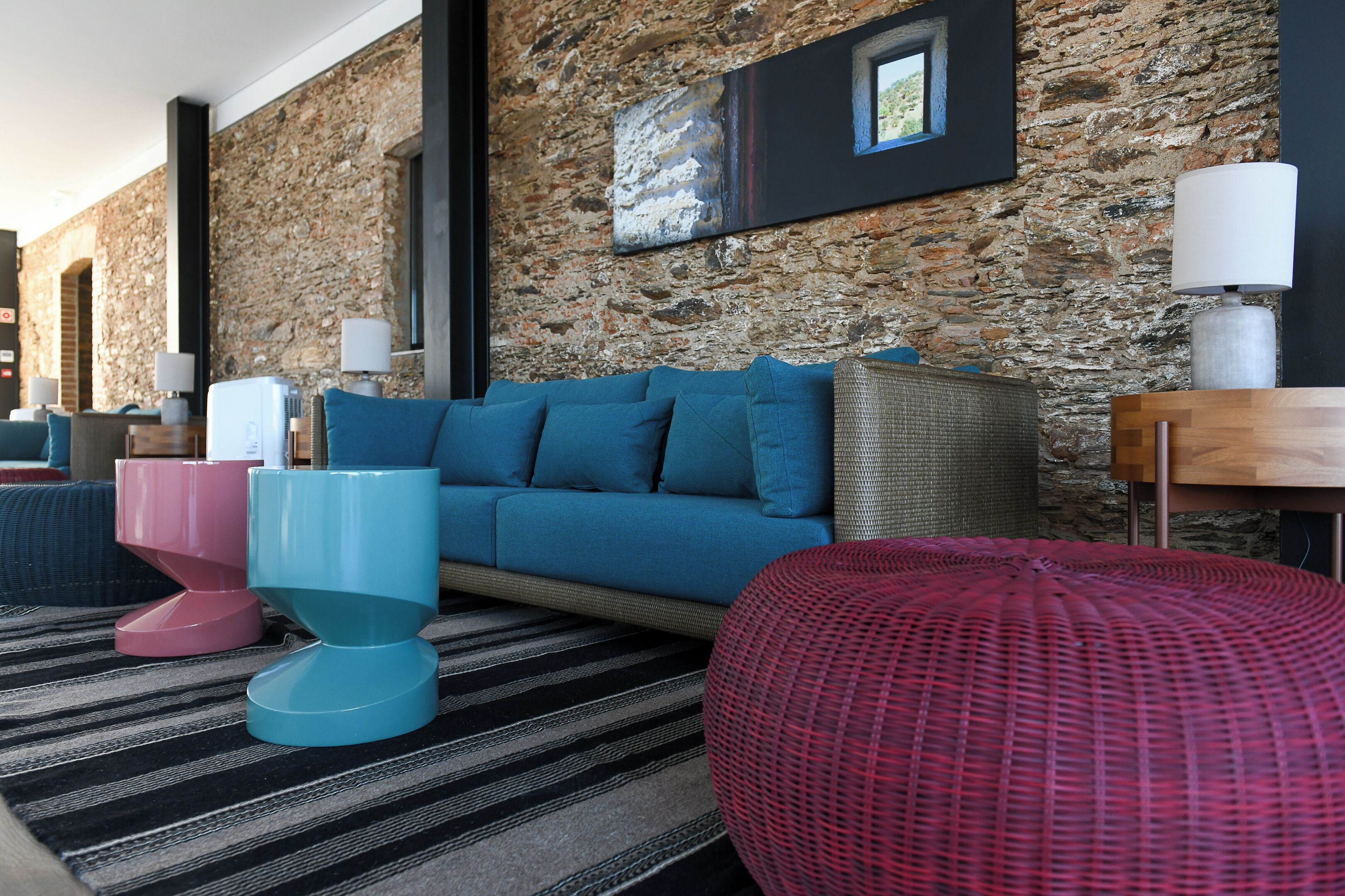 Uma sala de estar moderna com parede de pedra, um sofá azul e um banquinho vermelho.