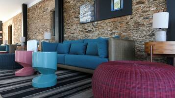 Uma sala de estar moderna com parede de pedra, um sofá azul e um banquinho vermelho.