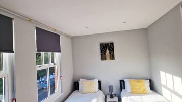 Quarto de hotel com duas camas, uma mesa pequena, uma mesa de cabeceira, um quadro na parede e uma janela com vista para o exterior.