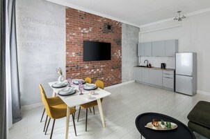 Cozinha moderna com televisão de tela plana, área de jantar com cadeiras amarelas e uma mesa pequena posta para dois.