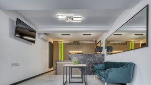 Uma área de recepção moderna, com balcão, sofá verde e televisão de tela plana na parede.