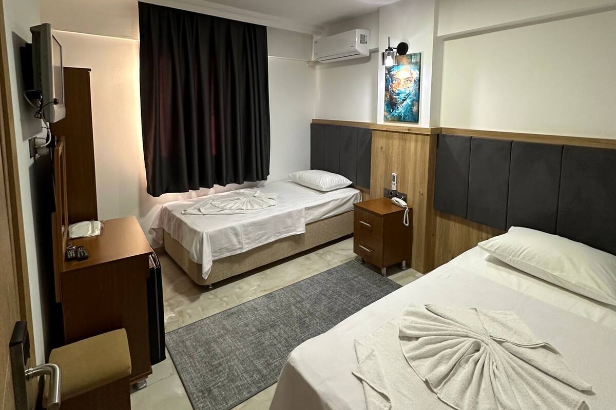 Quarto de hotel com duas camas, uma escrivaninha, uma cadeira, televisão, aparelho de ar condicionado e um quadro na parede.