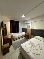 Quarto de hotel com duas camas, uma escrivaninha, uma cadeira, televisão, aparelho de ar condicionado e um quadro na parede.