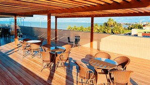 Pátio externo com mobiliário de vime e vista para o mar.