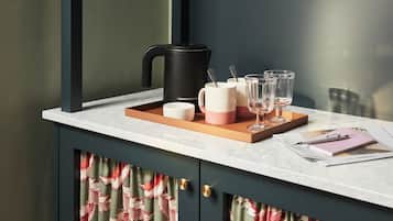 Uma bancada de cozinha com cafeteira, canecas, copos e uma bandeja.