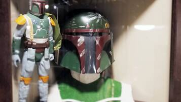 Uma vitrine com uma figura de um personagem em fato verde e branco, com capacete, e um capacete separado com design verde e vermelho.
