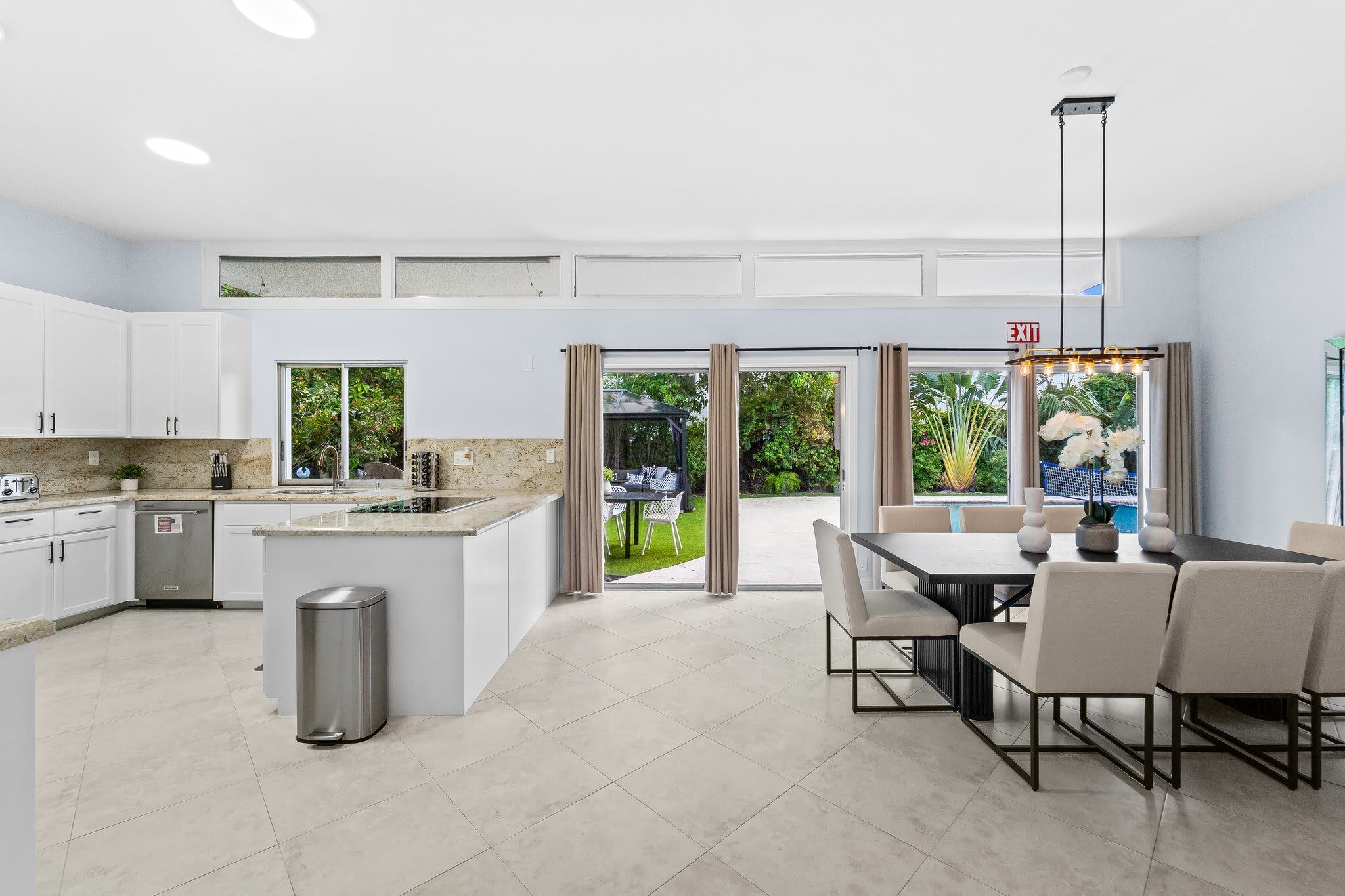 Uma cozinha moderna com armários brancos, uma ilha central e um espaço de jantar com mesa e cadeiras.