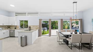 Uma cozinha moderna com armários brancos, uma ilha central e um espaço de jantar com mesa e cadeiras.