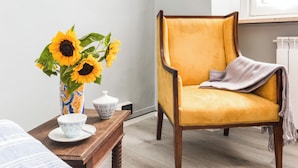Um quarto com uma poltrona amarela, uma mesa de madeira com um vaso de girassóis, uma xícara de chá e uma tigela azul e branca.