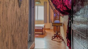 Corredor com parede de madeira, cama ao fundo, uma mesinha e porta com padrão.