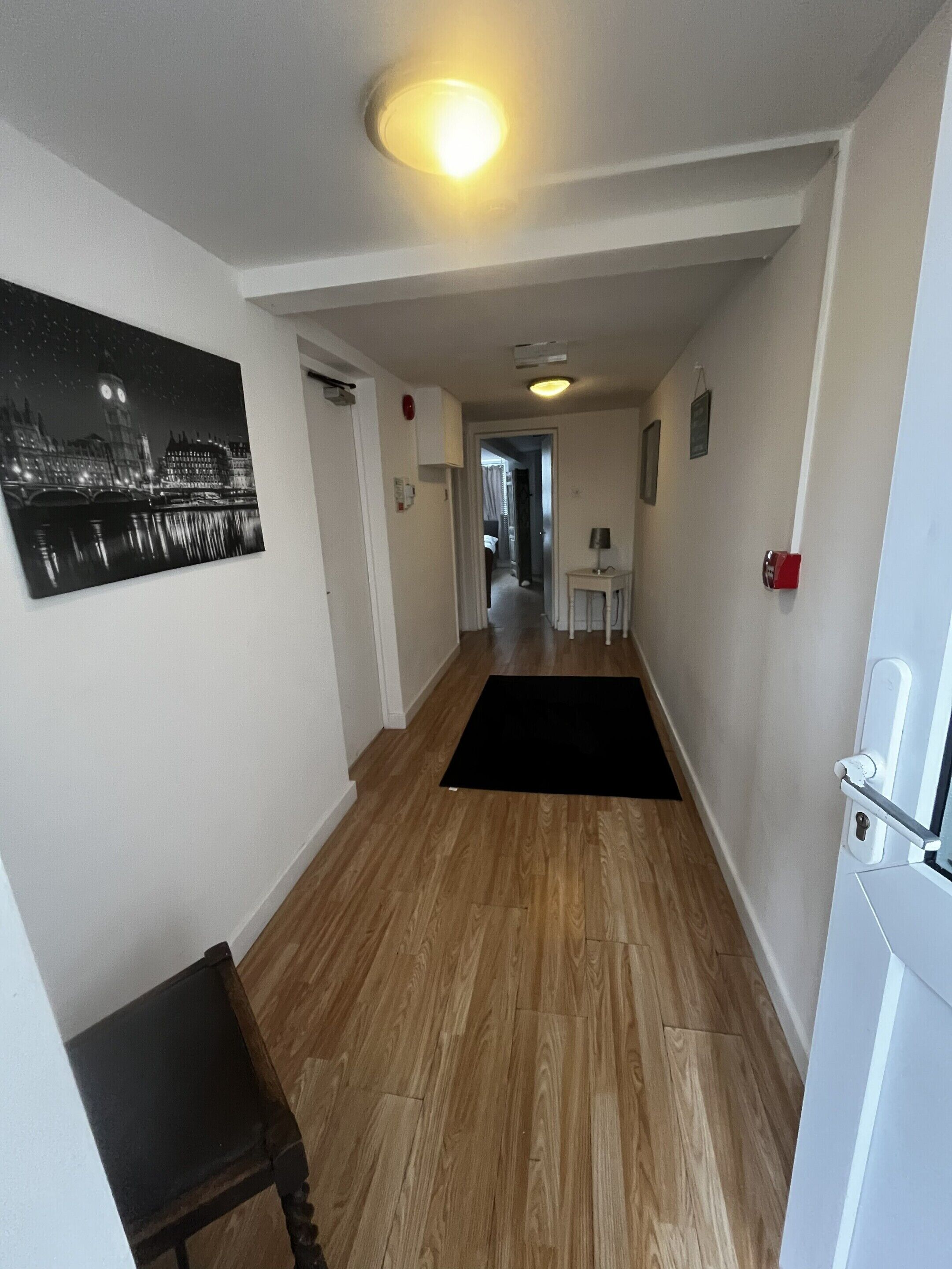 Um corredor com piso de madeira, um tapete preto, uma porta branca e uma cadeira preta.
