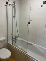 Um banheiro com chuveiro em box de vidro, vaso sanitário branco e banheira.