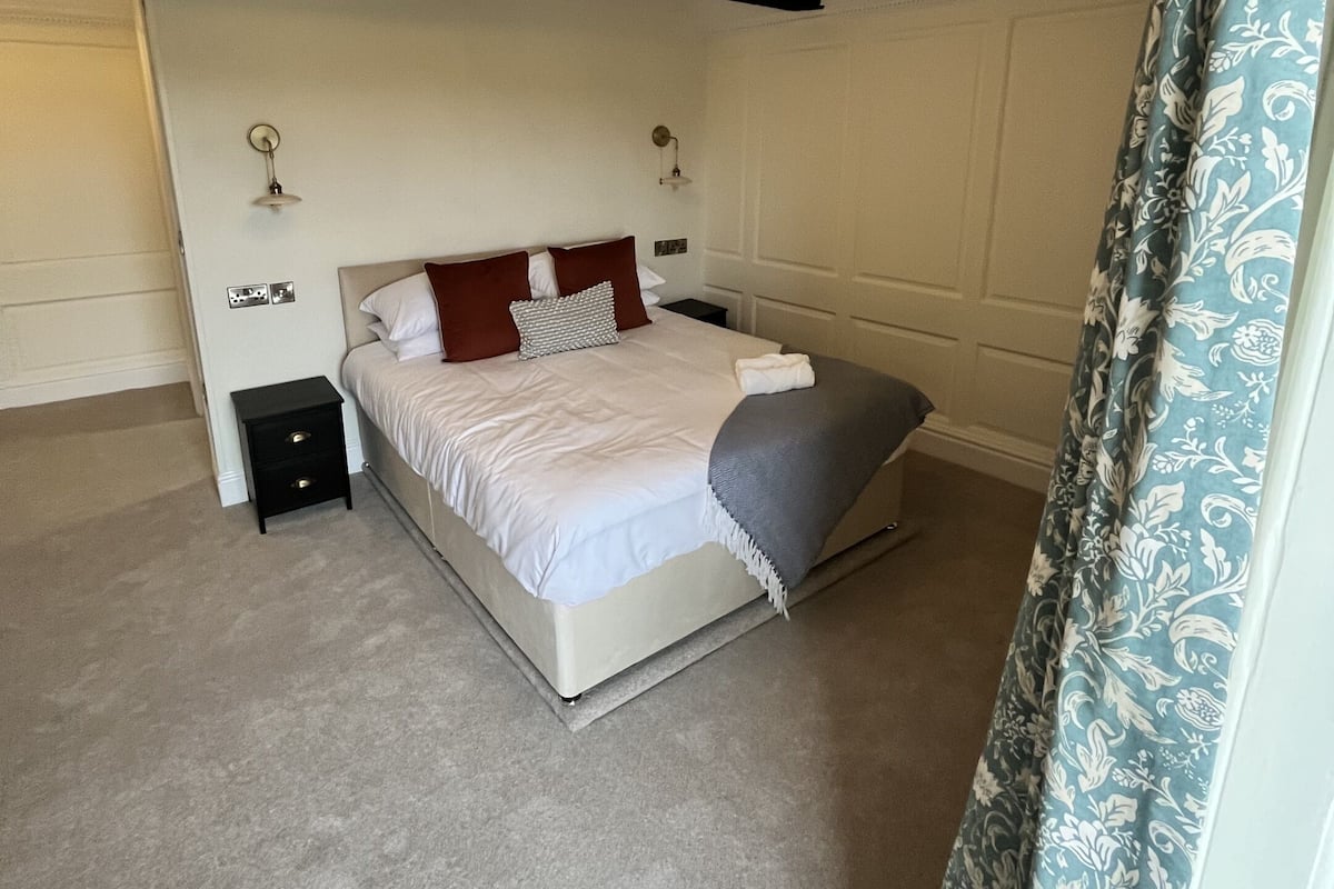 Quarto com cama, mesas de cabeceira, abajur e cortina estampada.