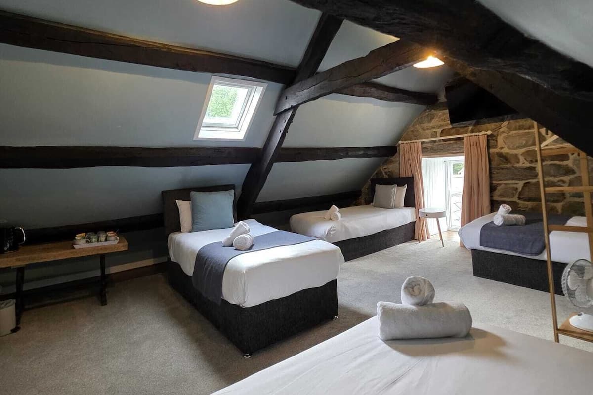 Um quarto de sótão aconchegante com três camas, uma escada de madeira e uma parede de pedra.