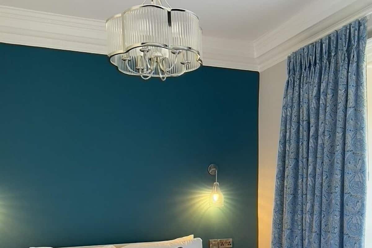 Cama bem arrumada com almofadas, mesa de cabeceira, um candelabro e janela com cortinas.