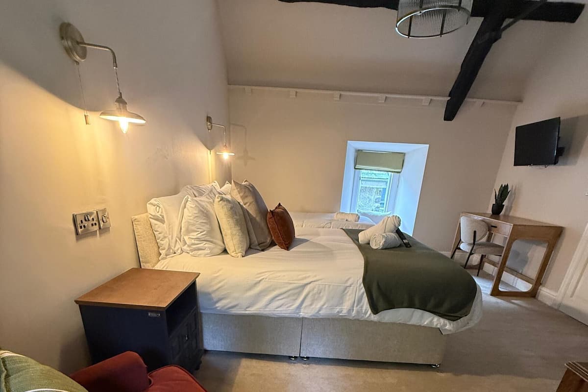 Quarto com cama, cadeira vermelha, mesa de madeira, luminária pendente e janela.