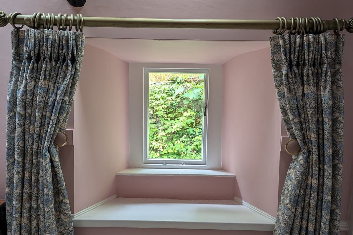 Um quarto com assento junto à janela, paredes cor-de-rosa e cortinas estampadas.