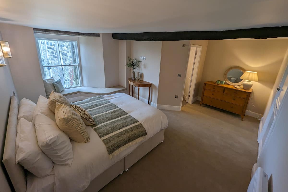 Quarto com uma cama grande, cômoda de madeira, mesa de cabeceira e janela com vista para um edifício de pedra.