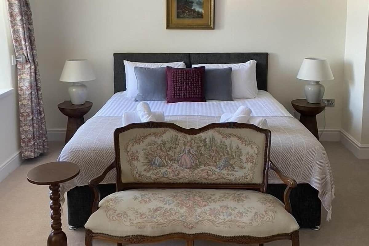 Um quarto com uma cama, duas mesas de cabeceira, uma cadeira, um candeeiro pendente e um quadro na parede.