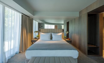 Quarto de hotel moderno com uma cama grande, uma mesa de cabeceira, uma luminária e um guarda-roupa.