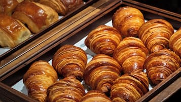 Exposição de diversos doces e pastelaria, incluindo croissants e outros produtos de panificação, dispostos em tabuleiros de madeira.