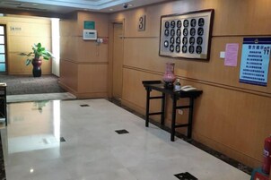 Um hall de hotel com balcão de recepção, uma planta, colagem de fotografias emolduradas e um quadro de avisos.