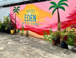 Um mural colorido com o texto 'HOSTAL EDEN' e 'Tu Casa en Ometepe' em uma parede de edifício, rodeado por vasos de plantas.